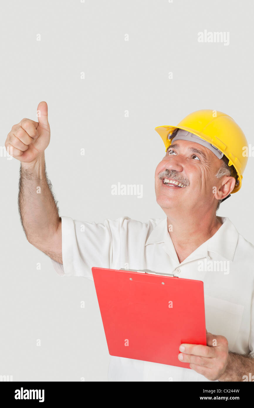 Happy senior constructor holding clipboard while gesturing thumbs up ...