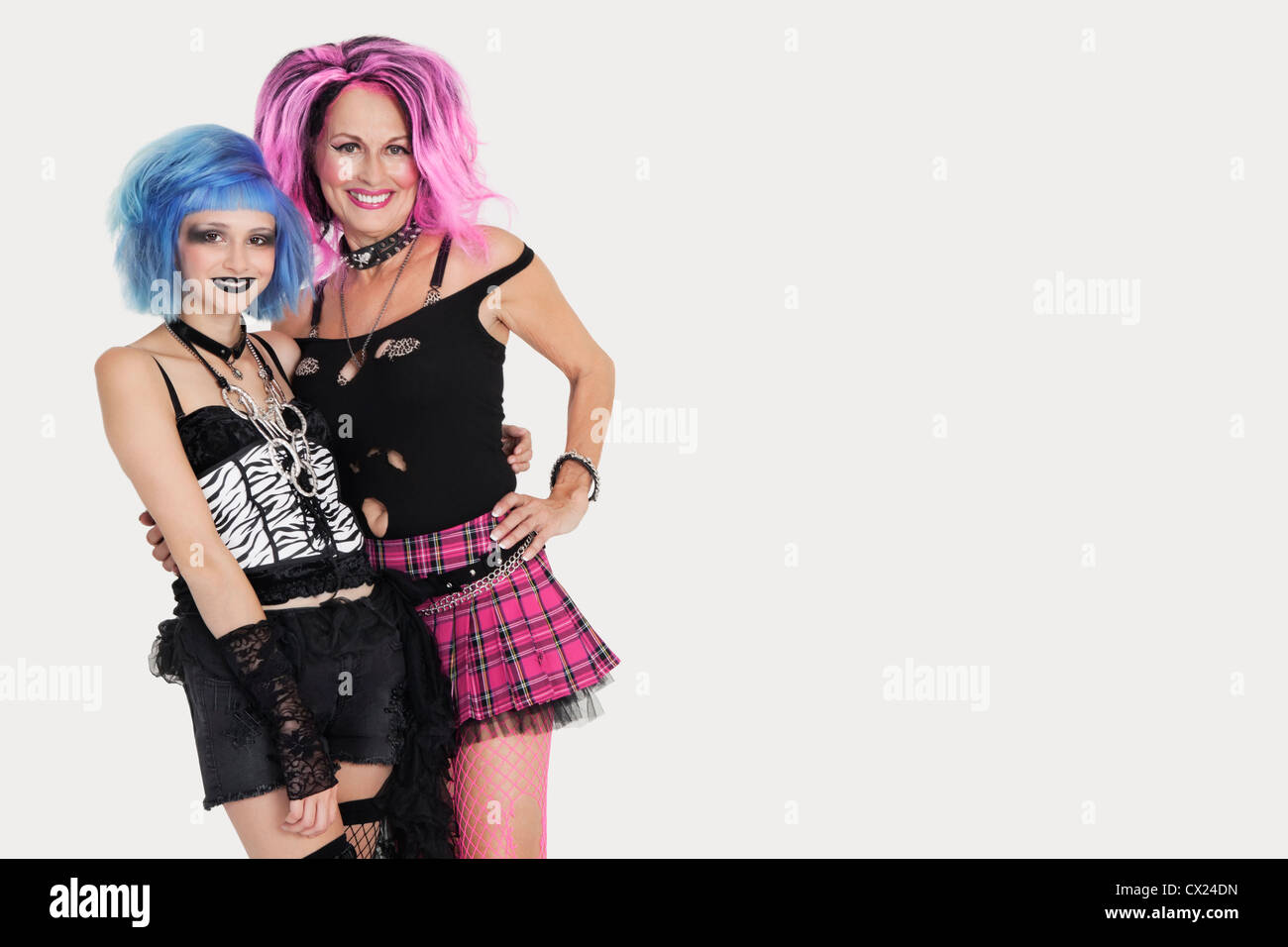 Portrait of punk females standing with arms around over gray background ...