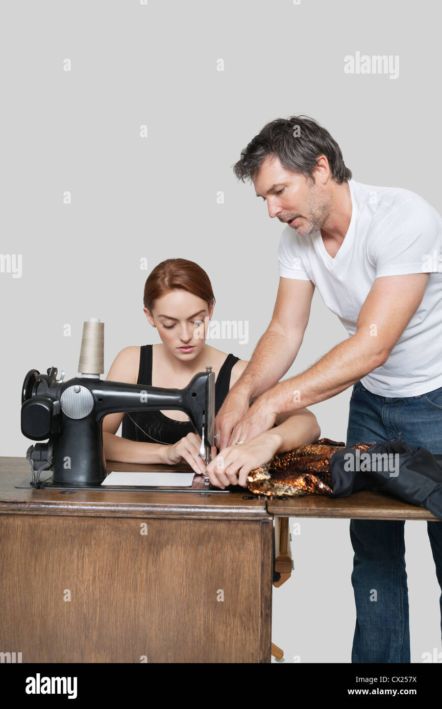 Designer helping coworker in stitching cloth on sewing machine over ...