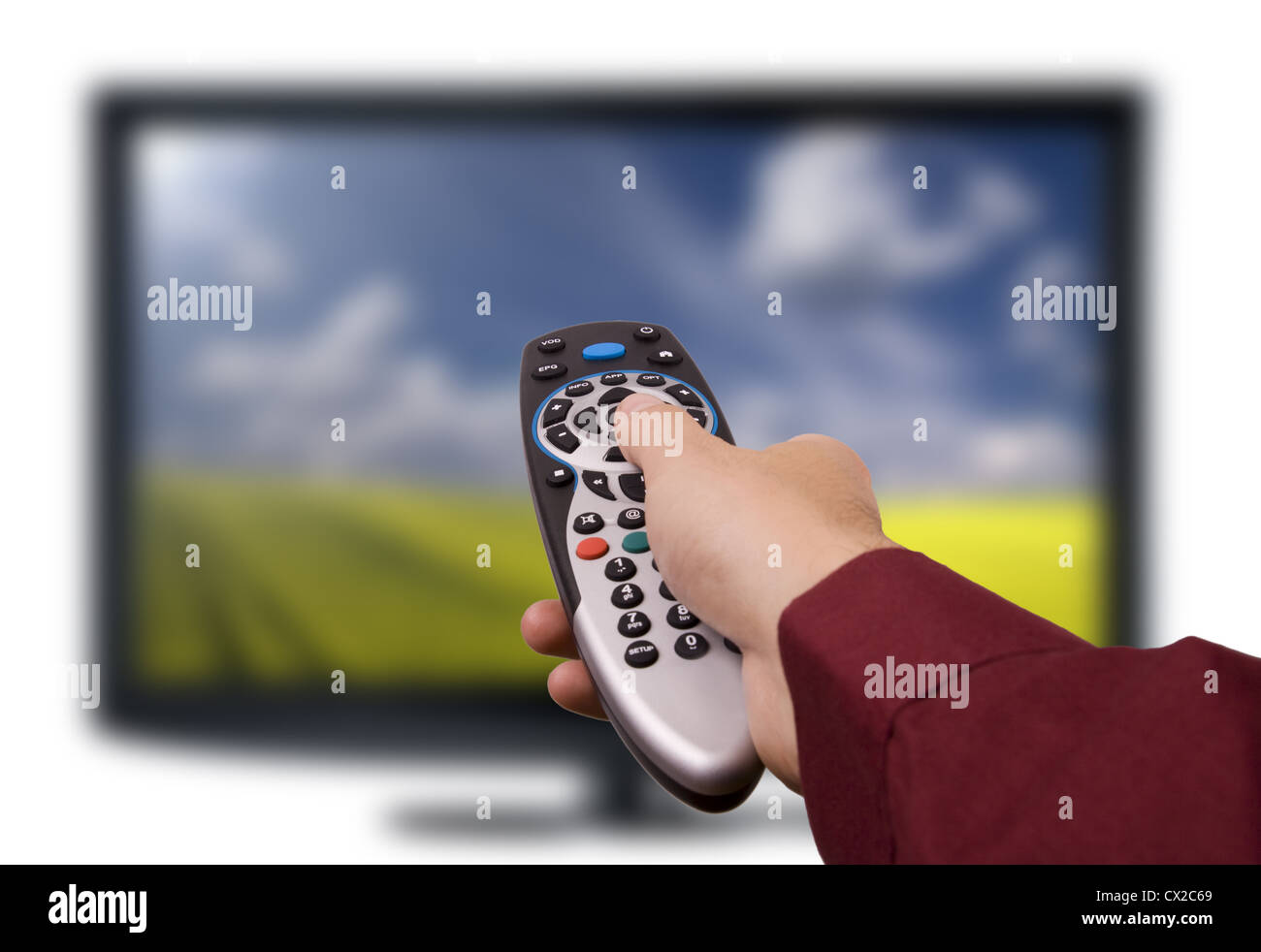 Hand holding TV remote control with a television in the background ...