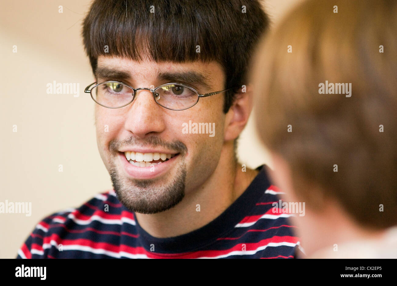 A young male student wearing glasses smiles during a college class ...