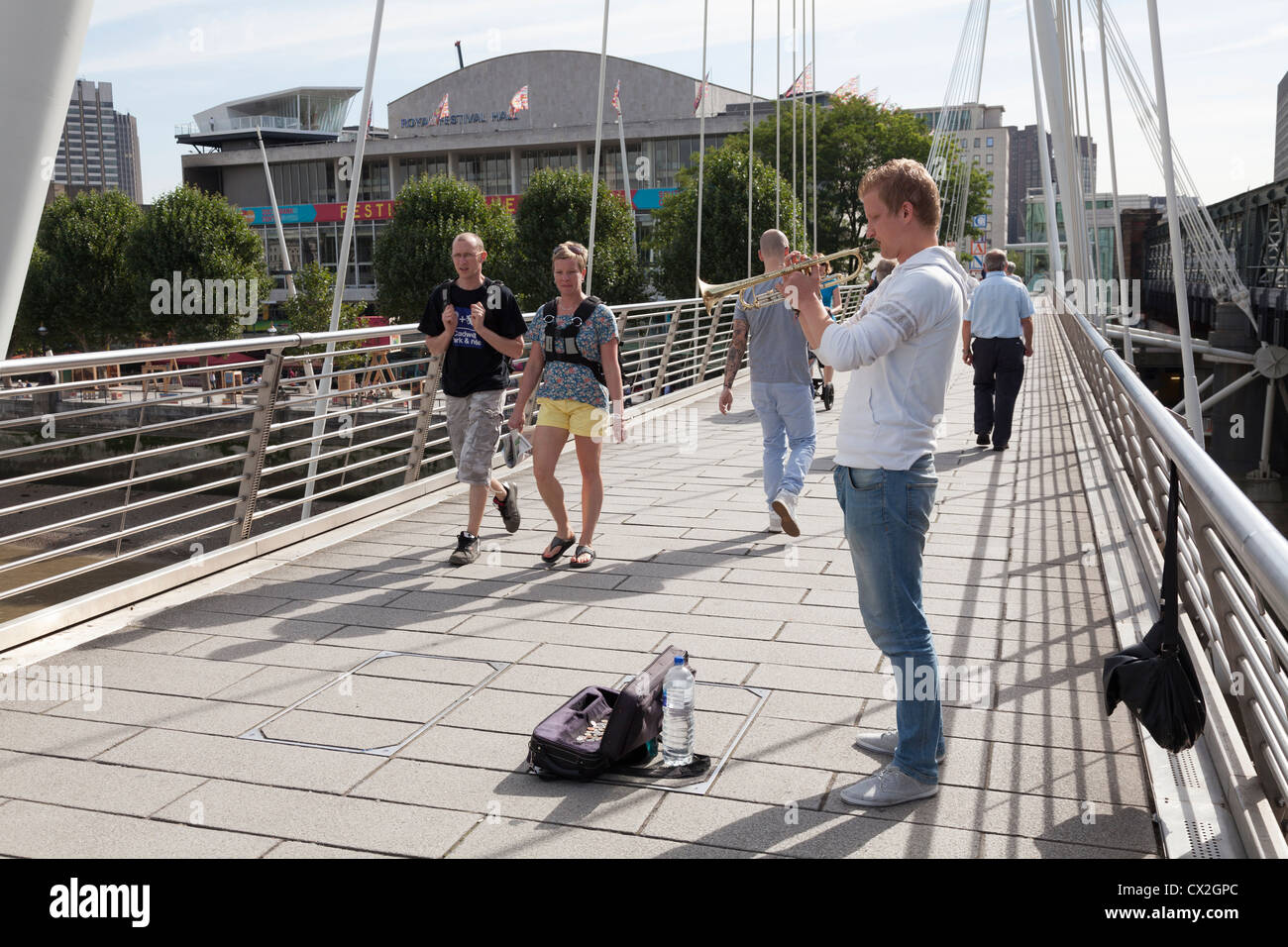 Busker playing trumpet on the Golden Jubilee pedestrian Bridge over the ...