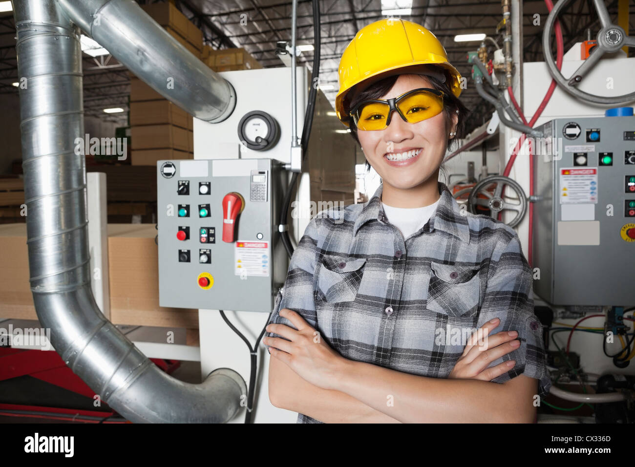 Portrait of female industrial worker smiling while standing in factory ...