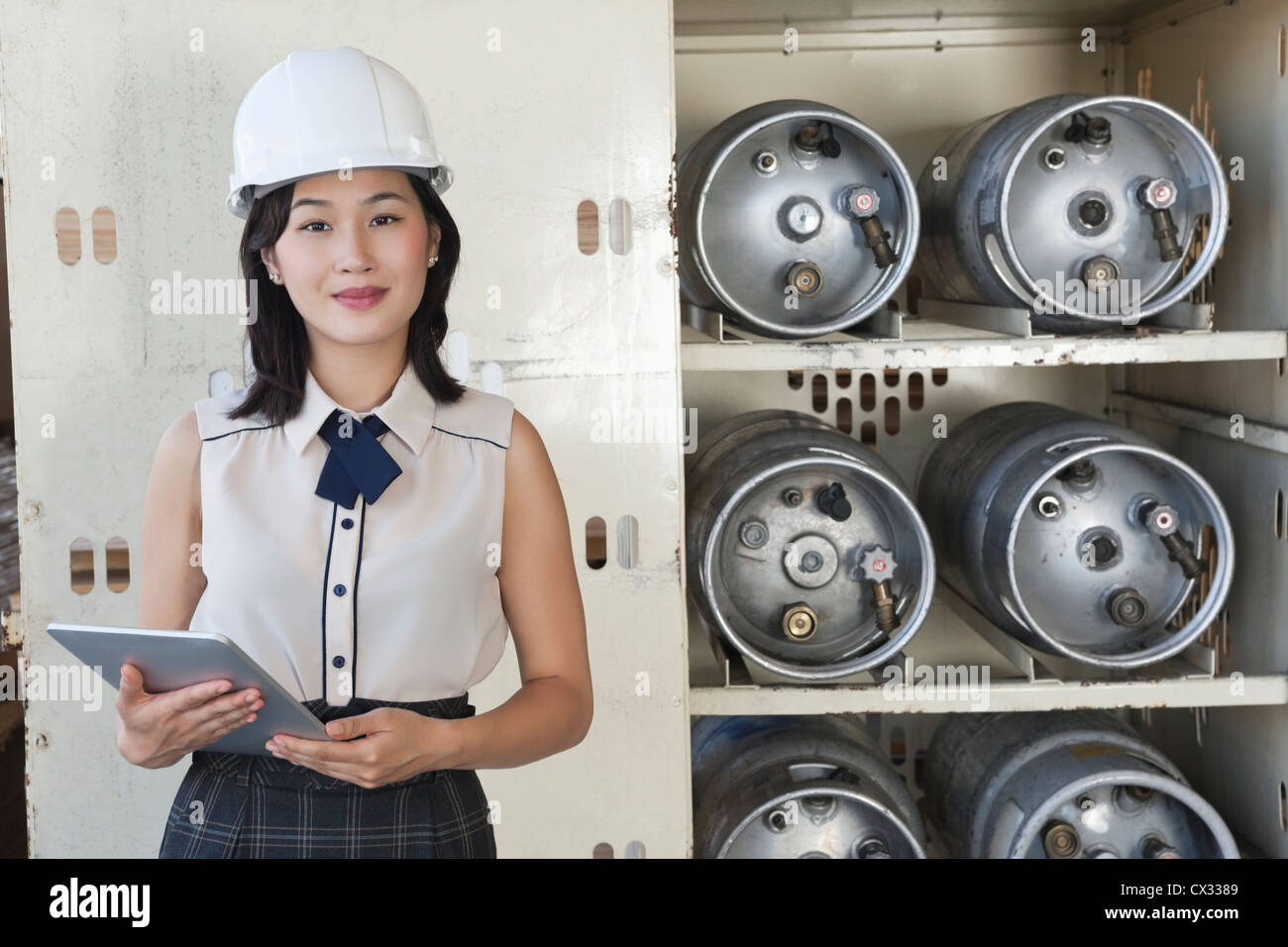 Portrait of female industrial worker holding tablet PC with cylinders ...