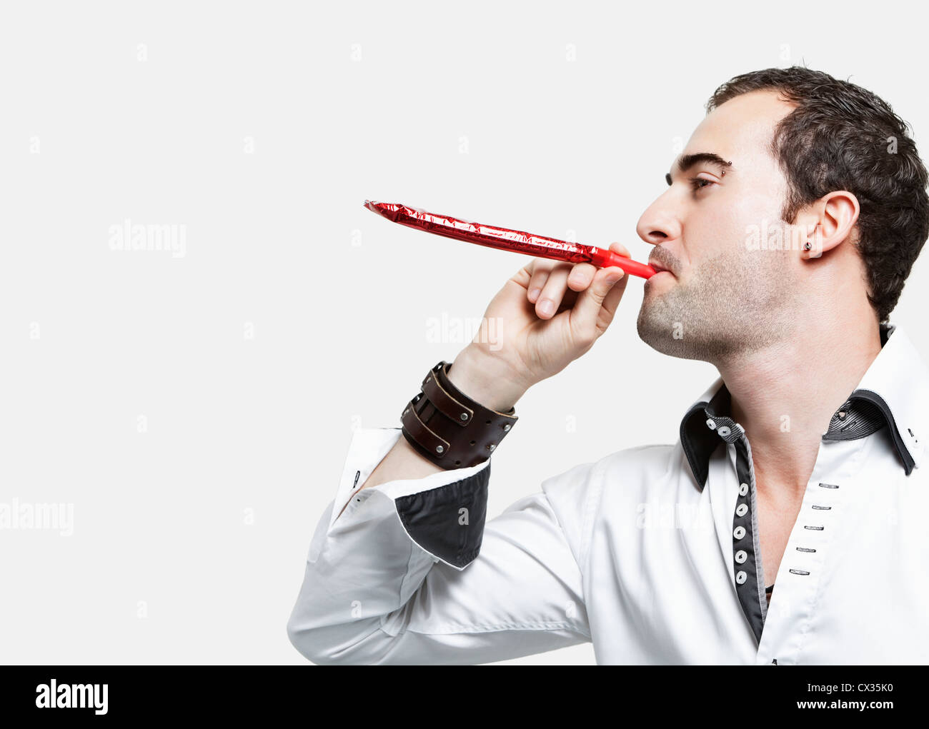 Young man blowing party blower against gray background Stock Photo - Alamy