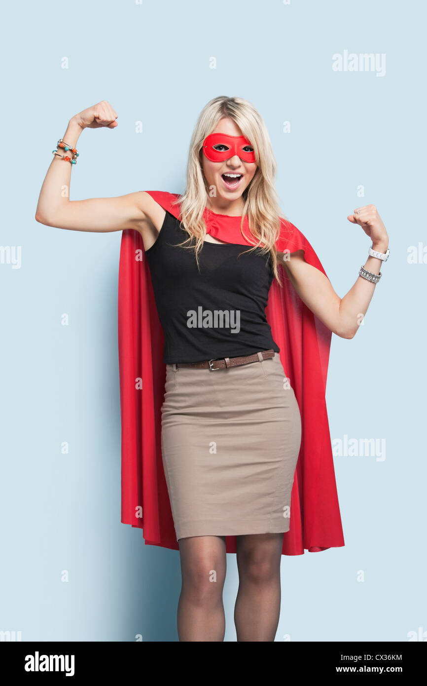 Portrait of excited young blond woman in superhero costume flexing arms ...