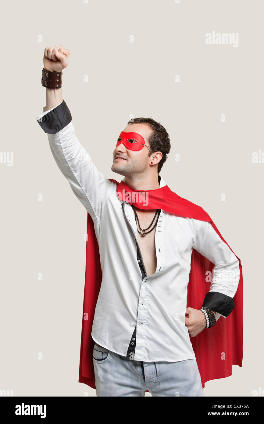 Young man in superhero costume with hand raised against gray background ...