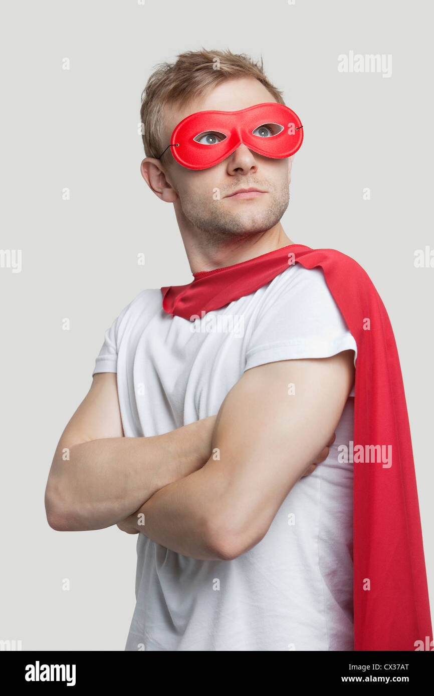 Young man in red superhero costume looking up over gray background ...
