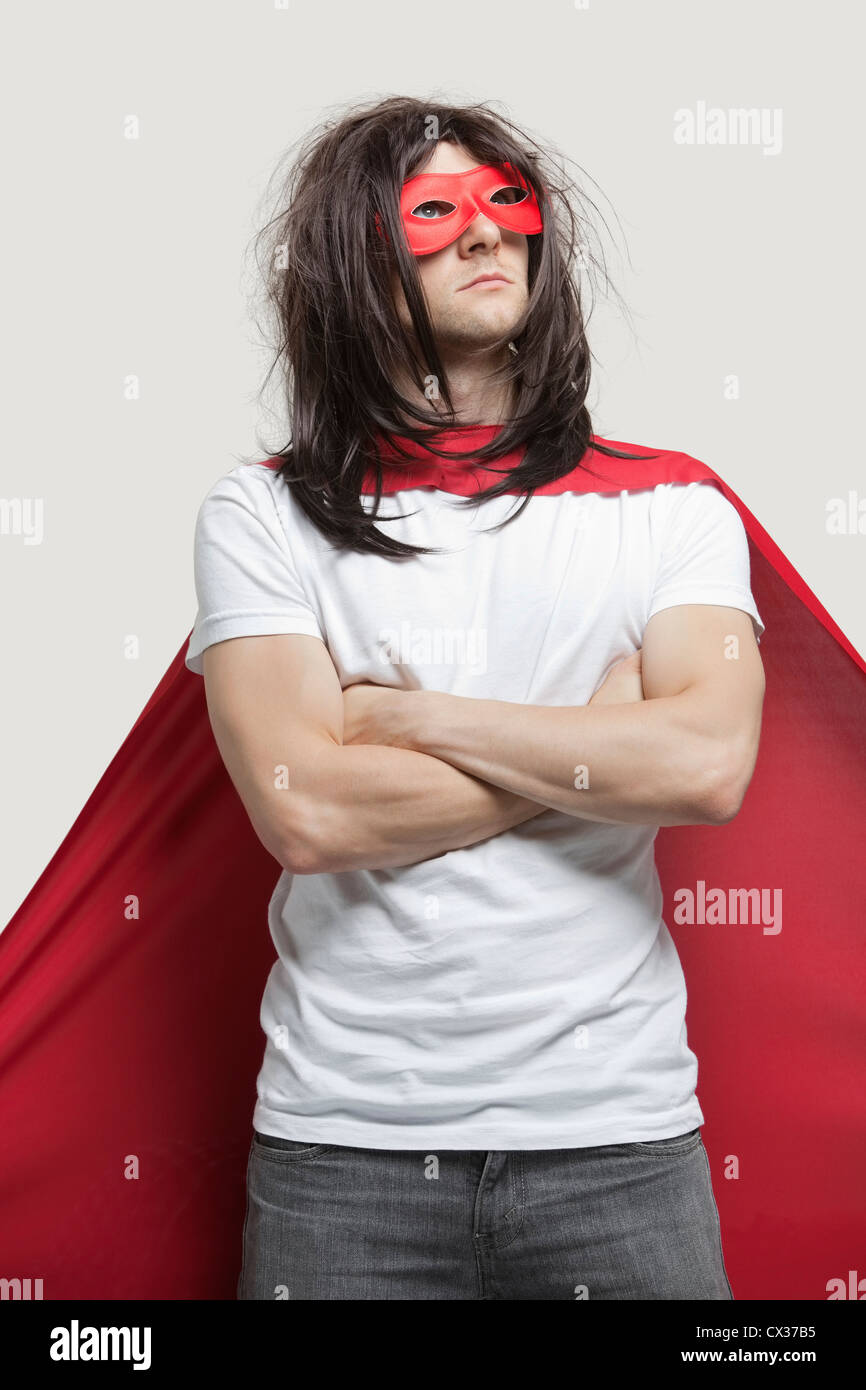 Young man in super hero costume standing with arms crossed against gray ...