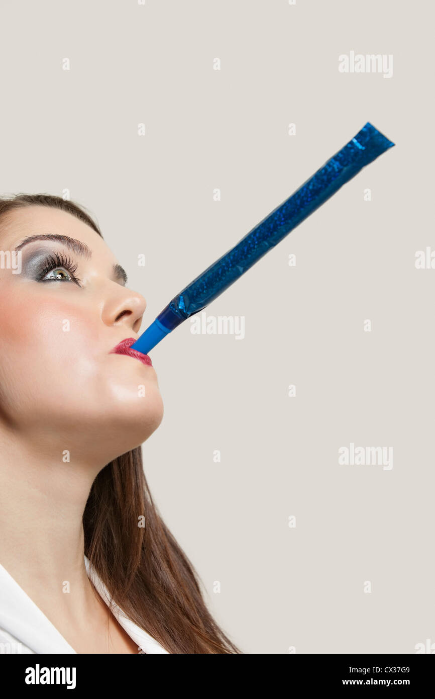 Close-up of a young woman blowing blue party blower against gray ...