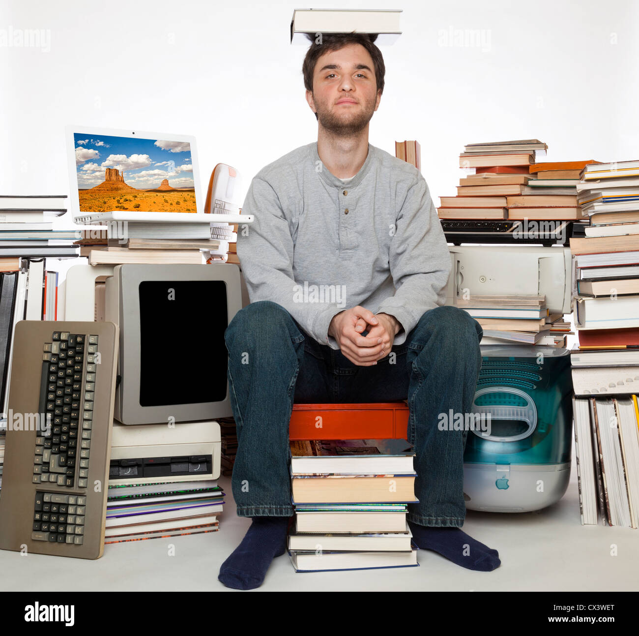 A young lady sits and poses with a pile of books and computers ...