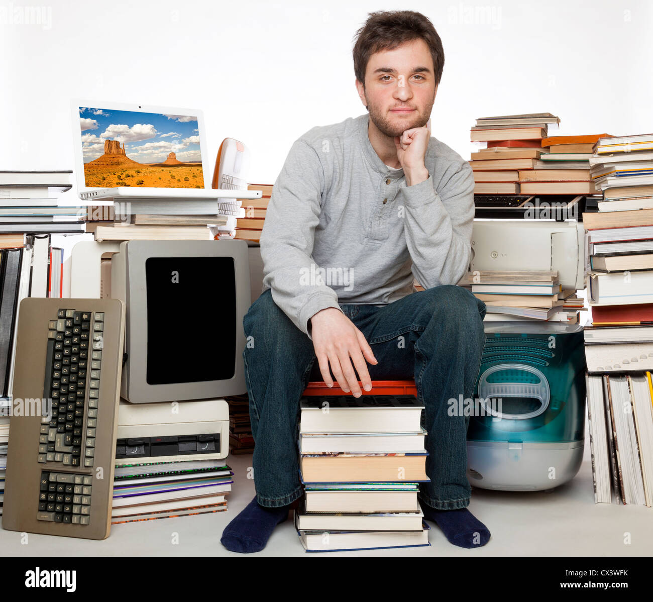 A young lady sits and poses with a pile of books and computers ...
