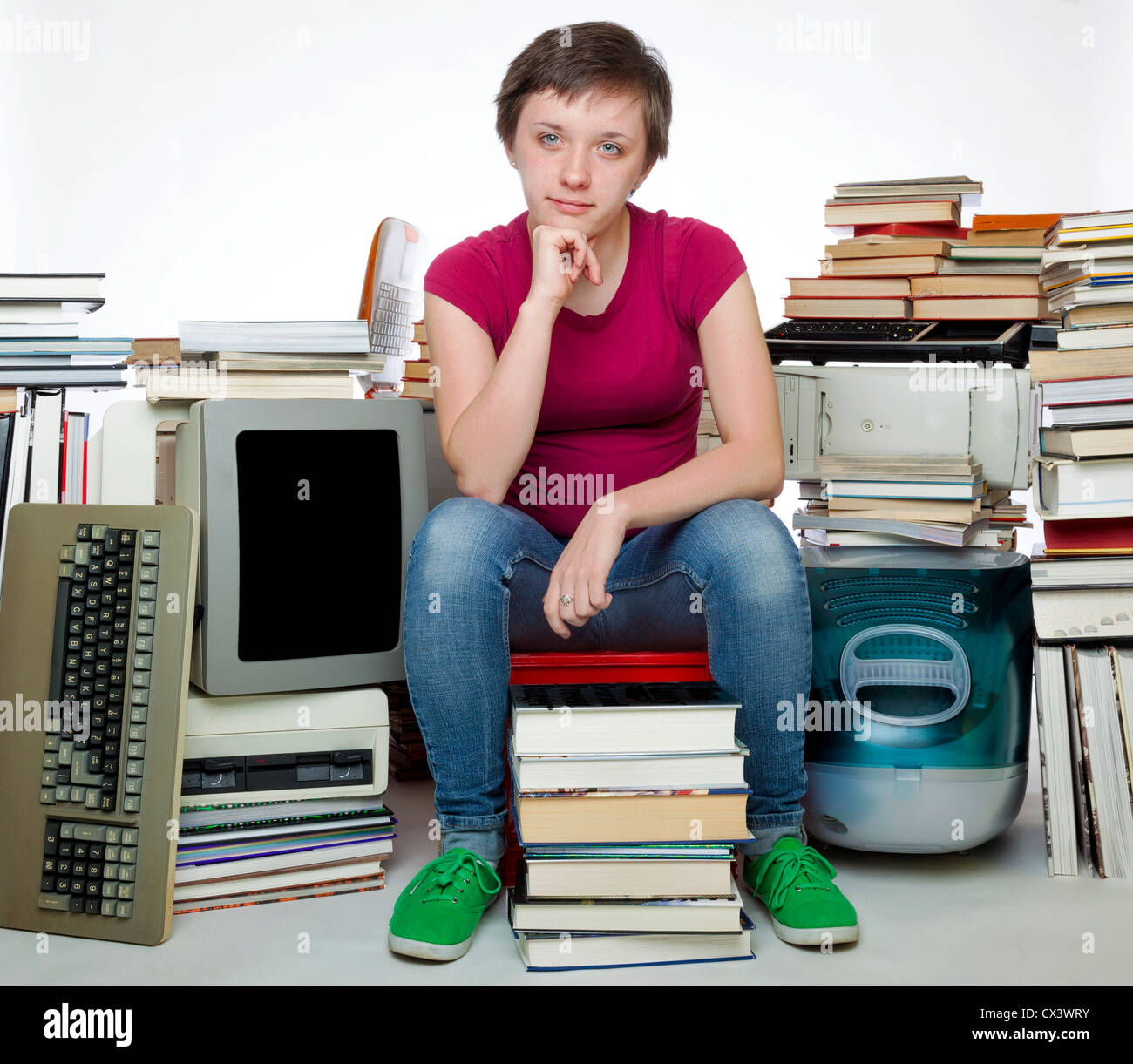 A young lady sits and poses with a pile of books and computers ...