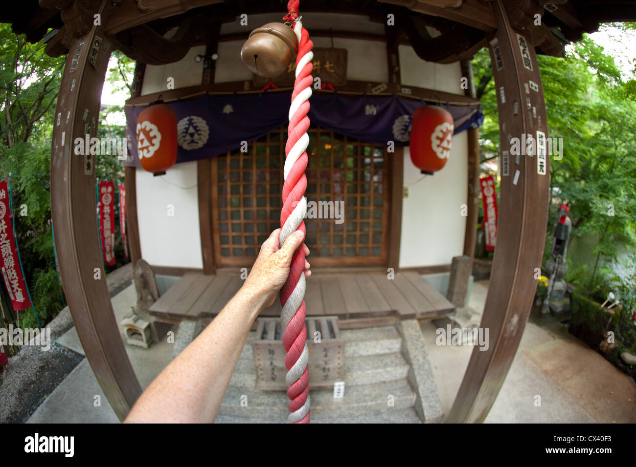 Arm reaching out to pull rope and ring bell at a Buddhist shrine in ...