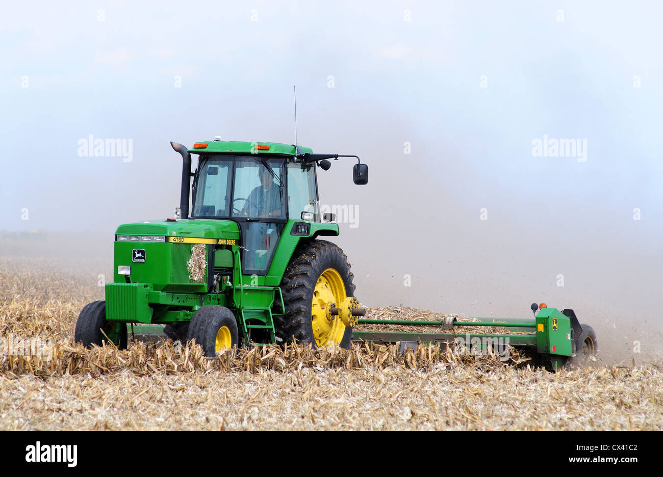 A John Deere farm tractor tilling or cultivating a farm's corn field ...