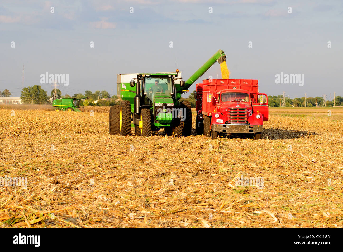 Harvesting corn with a John Deere combine and tractor hauling grain wagon and offloading the ...