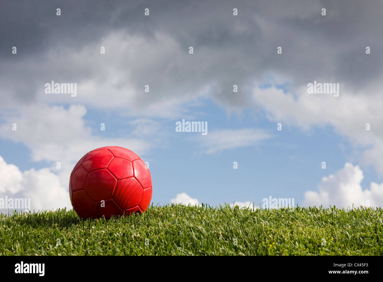 A football red ball on the grass with a cloudy sky Stock Photo - Alamy