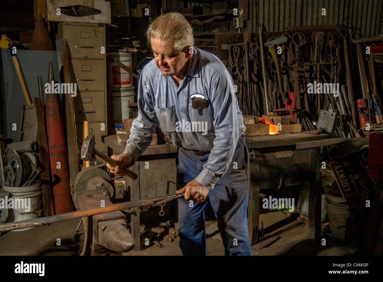 An elderly blacksmith in a Tustin, CA, barn built in 1912 hammers a red ...