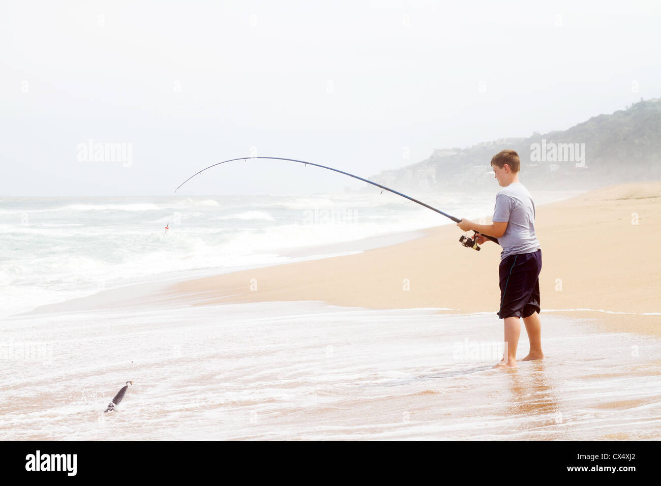 teen boy pulling a fish out of water with fishing rod on beach Stock ...