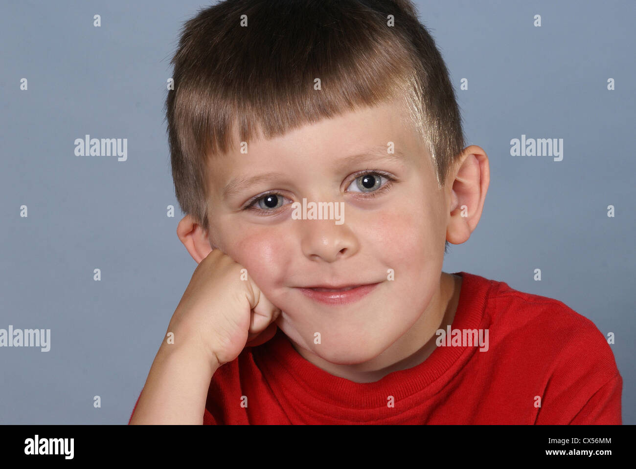 Young boy posing with a smile on his face and cheek resting on his fist ...