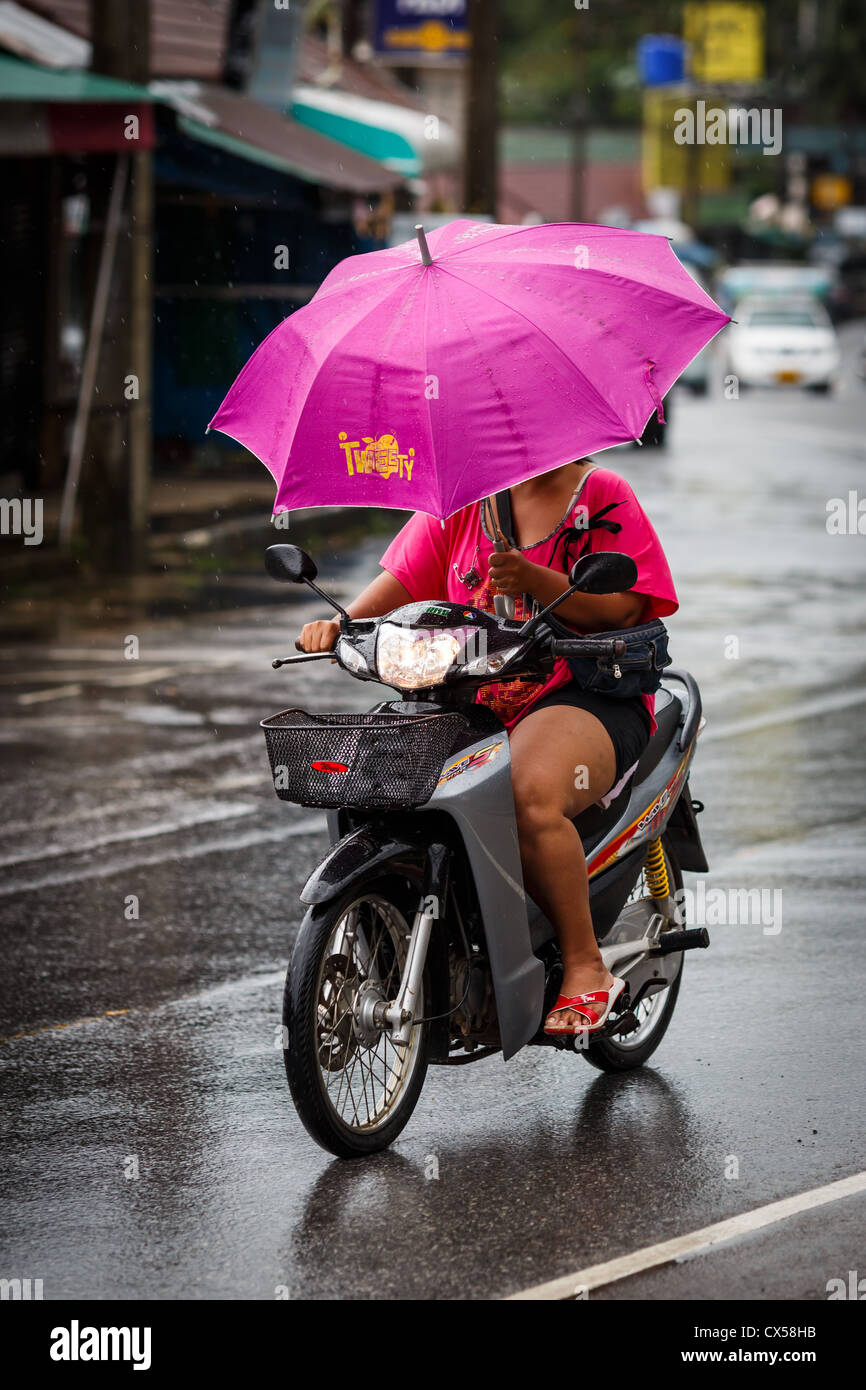 Female riding a motorbike with an umbrella in one hand, Koh Chang ...