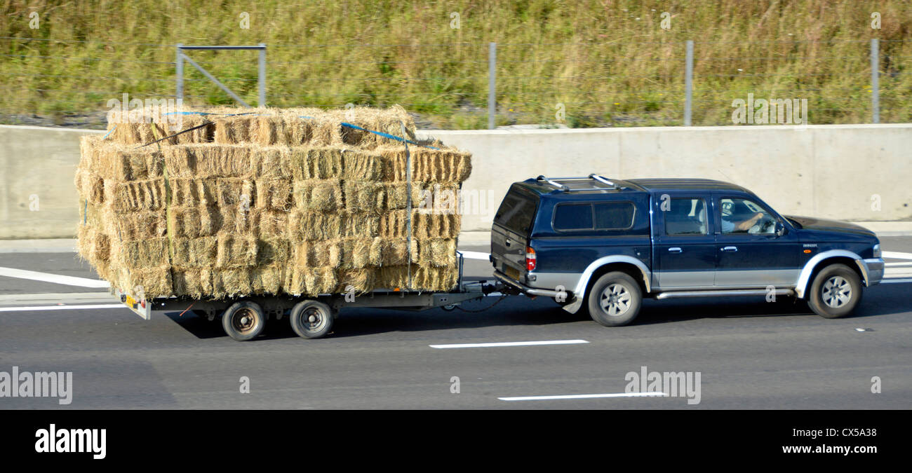 Trailer loaded with bales of hay being towed by car driving along M25 ...