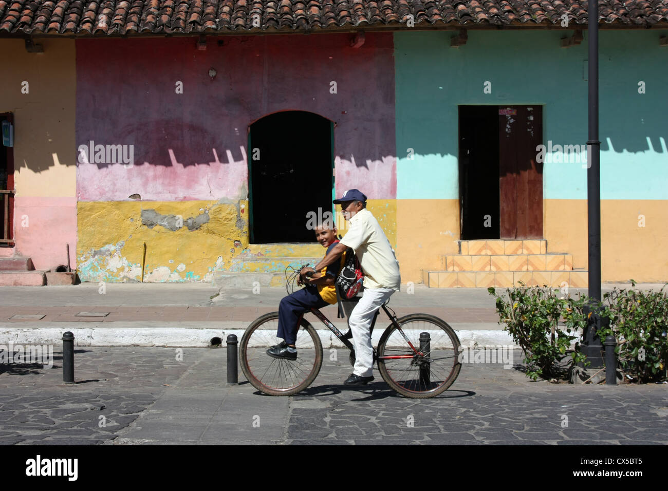 Man and child on bicycle ride past run down houses in the city of ...