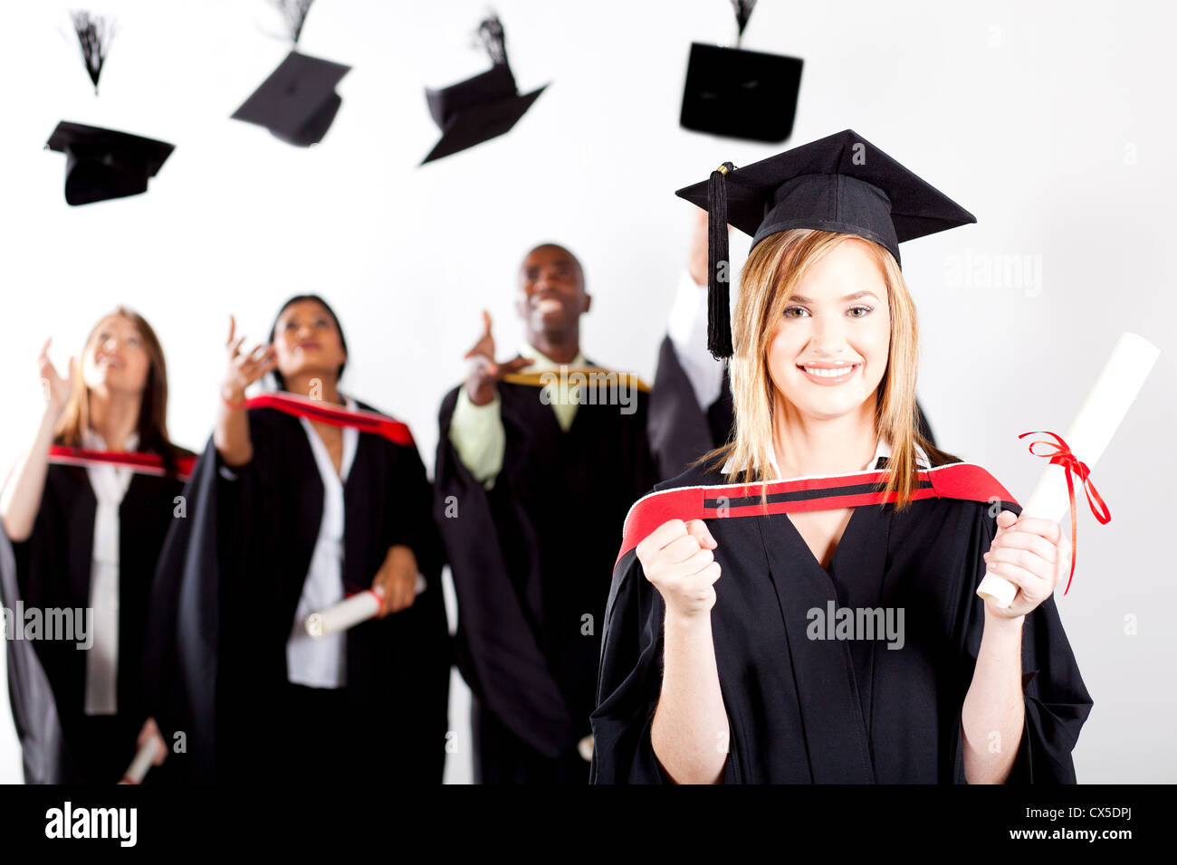 happy female graduate at graduation with classmates throwing caps in ...