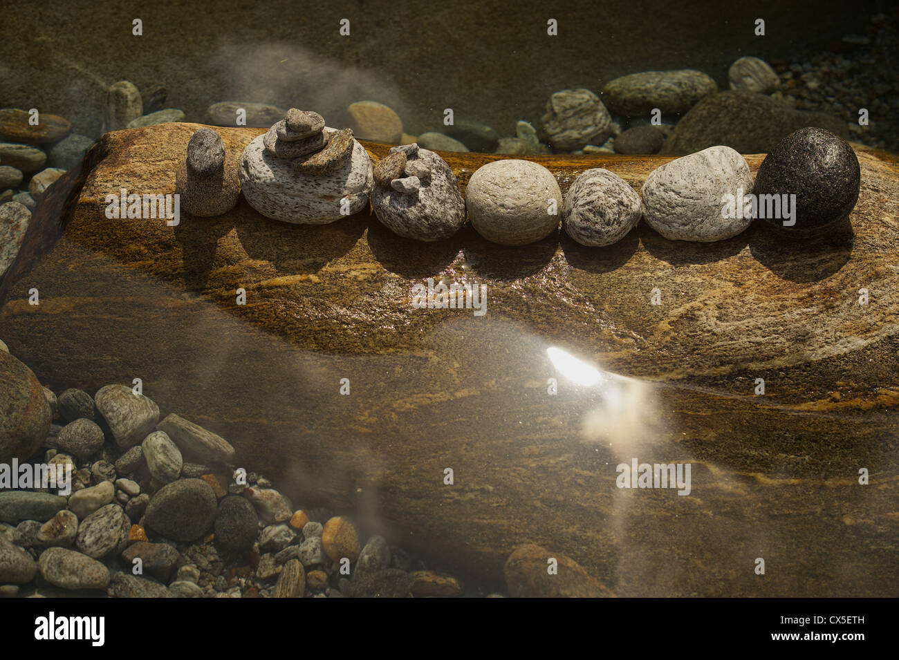 Stones in a row on a mother rock in water with sun shining through the ...