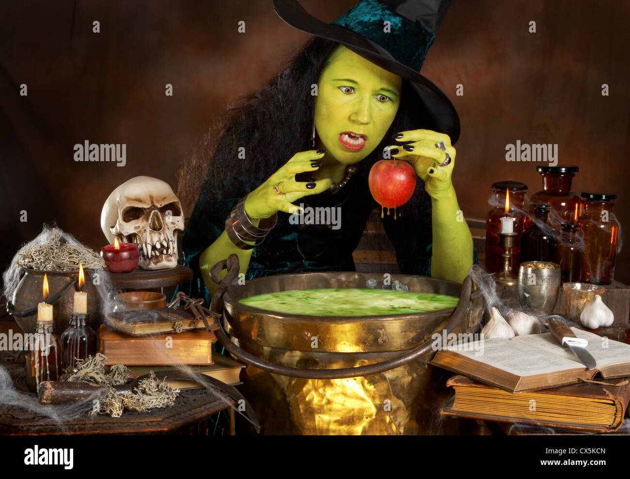 Green halloween witch putting a red apple in a cauldron with poisonous ...