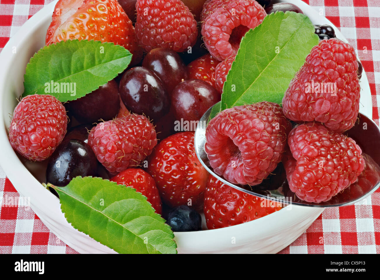 Bowl of berries on a Gingham tablecloth with raspberries in a spoon ...