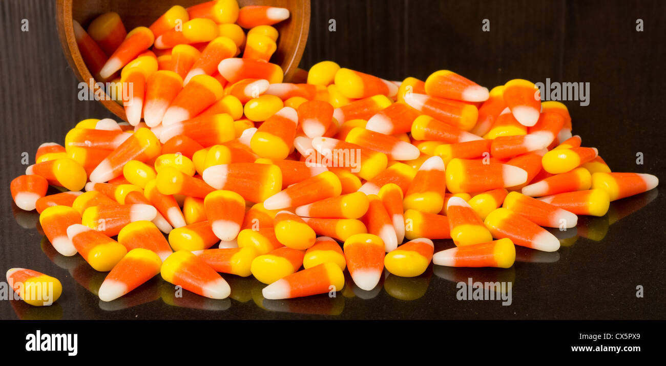 Candy corn spilling from wooden bowl onto black table Stock Photo - Alamy