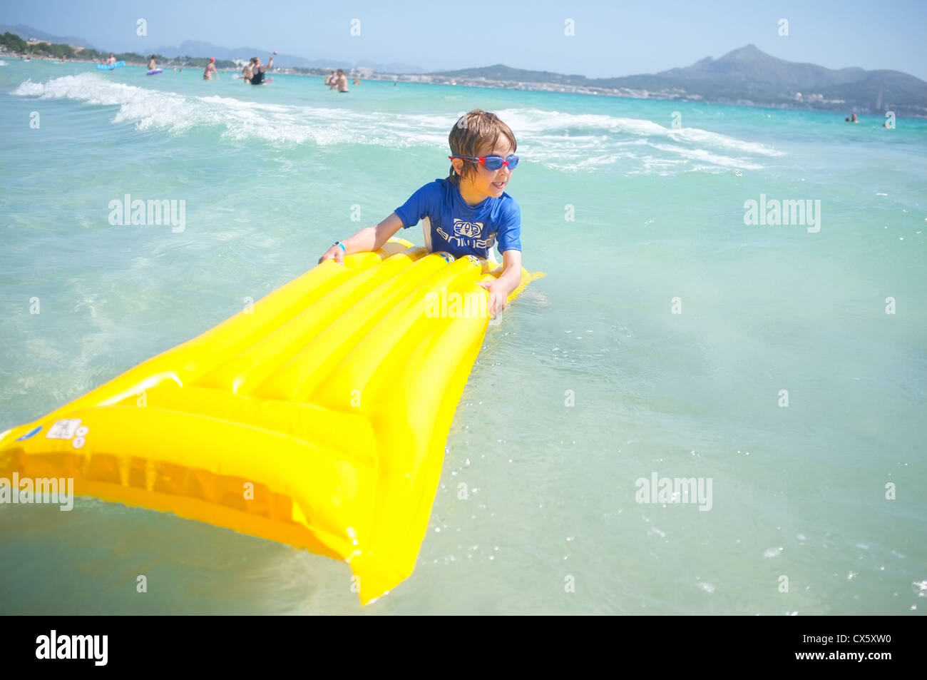 a young boy having fun playing in the surf on a inflatable raft lilo ...