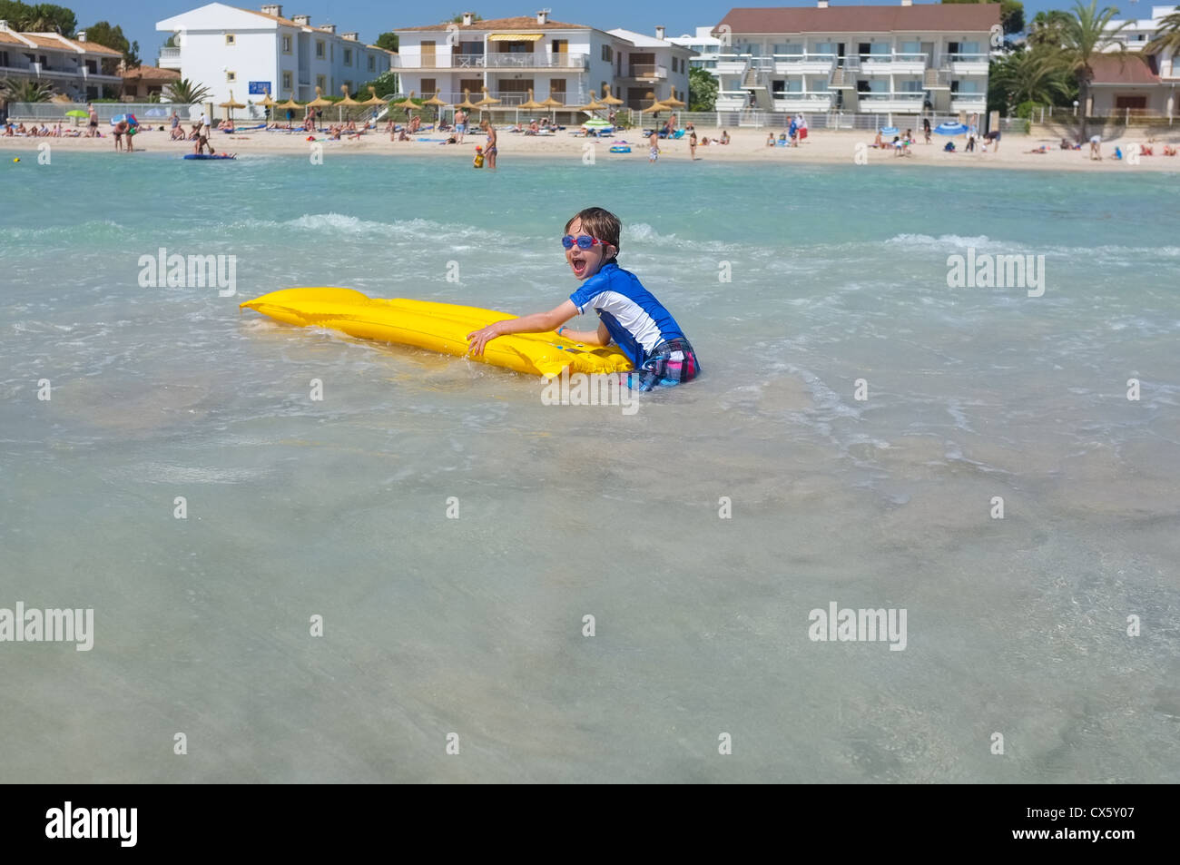 a young boy paddles in the warm sea on a inflatable yellow lilo raft ...