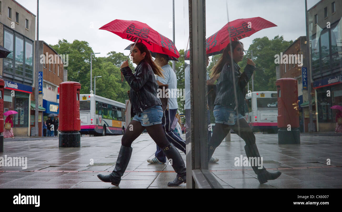 shoppers walking in the rain with umbrellas reflected in a shop window ...