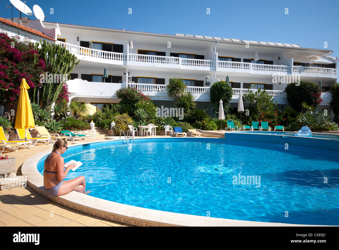 ALGARVE, PORTUGAL. A woman reading a book by the side of a hotel pool ...
