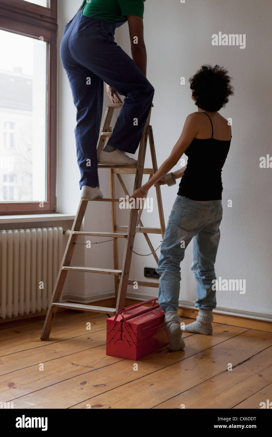 A woman holding a ladder while a man steps up Stock Photo - Alamy