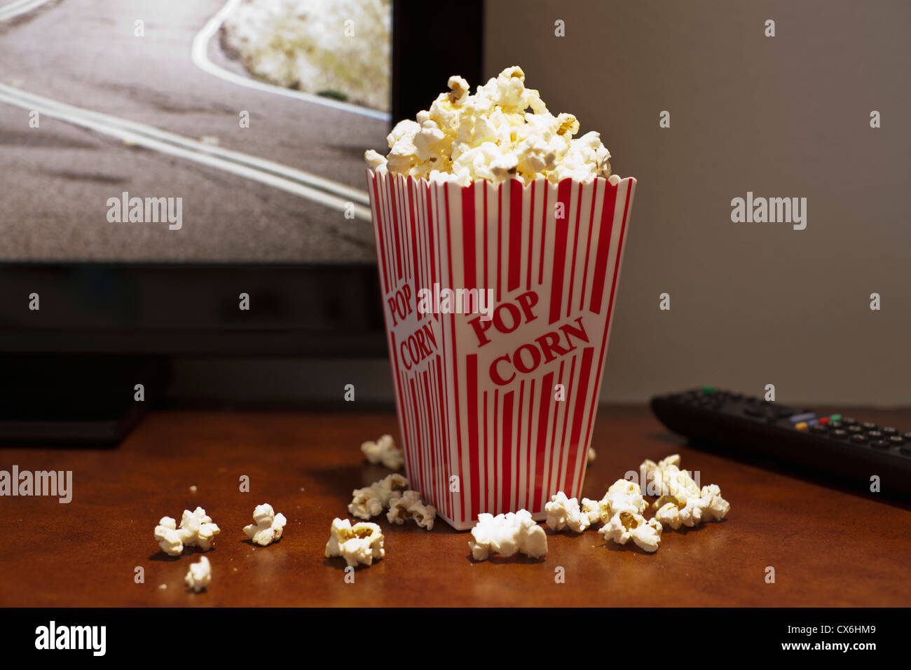 A red striped carton of popcorn on a table in front of a flat screen TV ...
