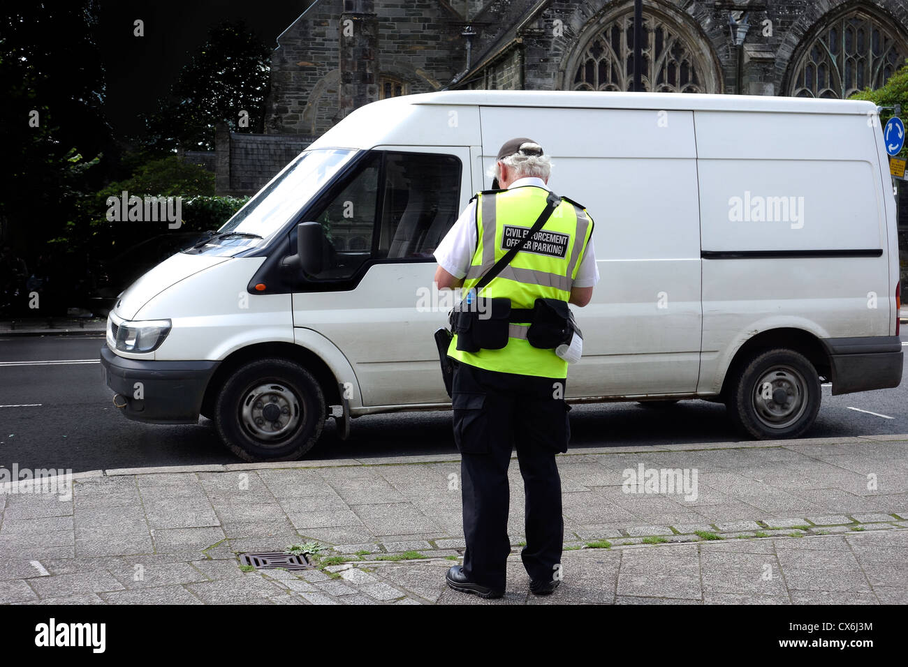 Traffic warden (civil enforcement officer parking) at work on white van ...