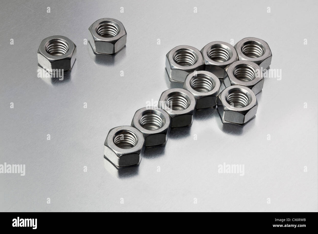 Two metal nuts next to a group of nuts arranged into an arrow sign ...