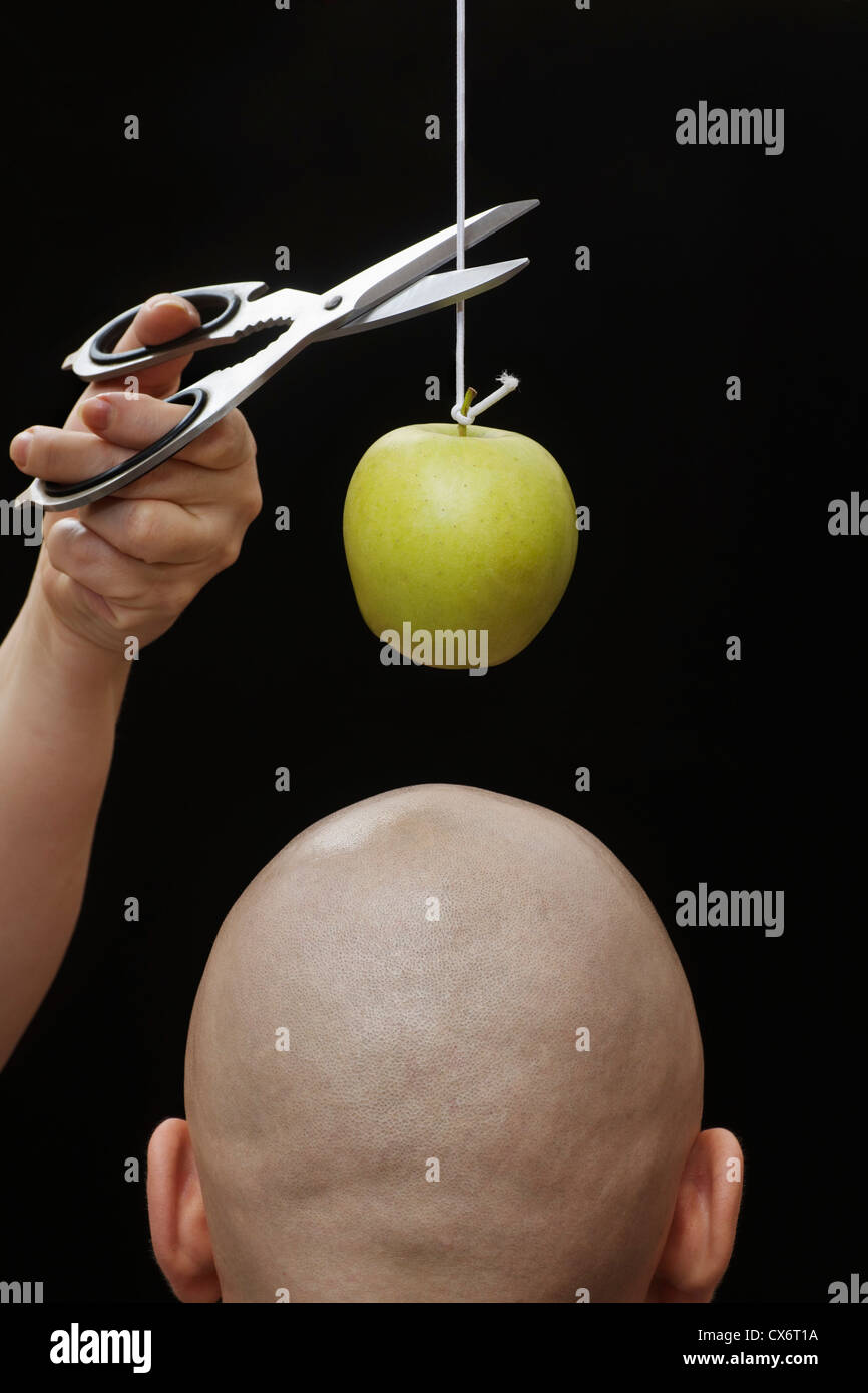 A woman cutting an apple on a string above the head of a man Stock ...
