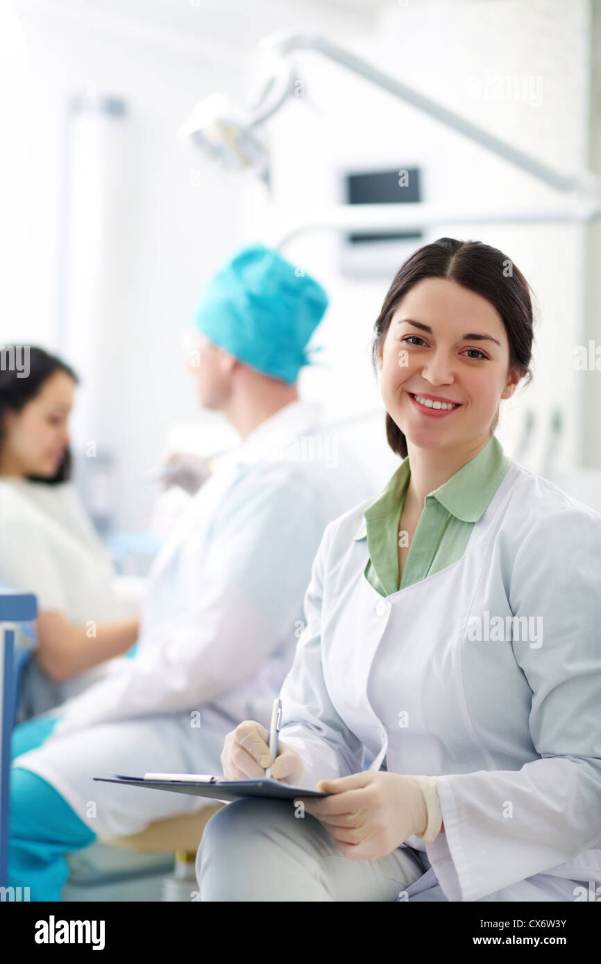 Pretty nurse looking at camera with smile on background of dentist and ...