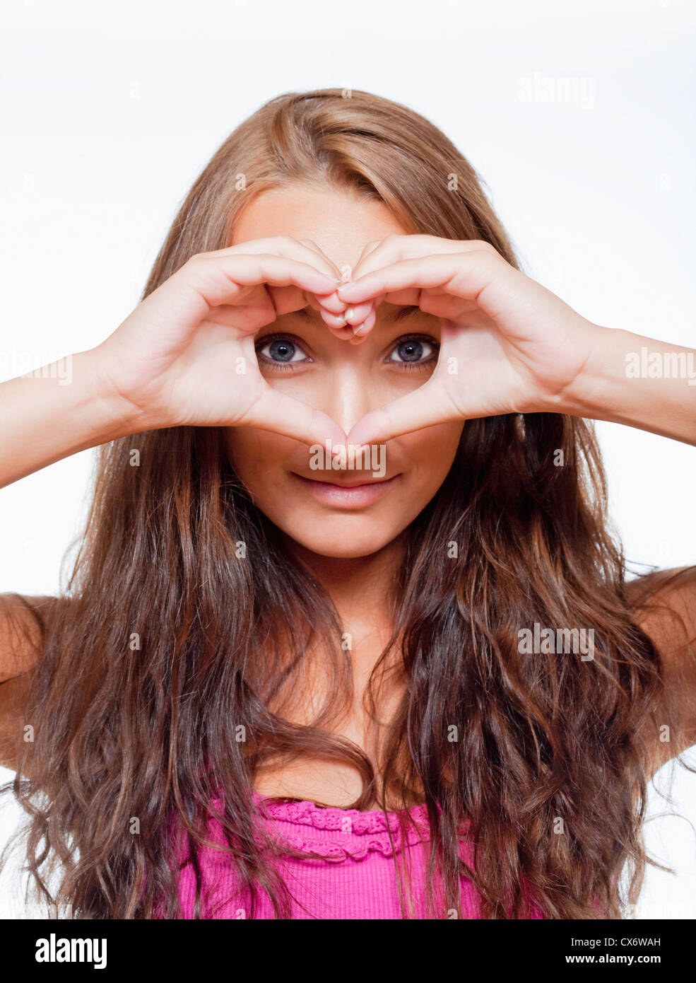 young girl looking through a heart shape formed by her fingers ...