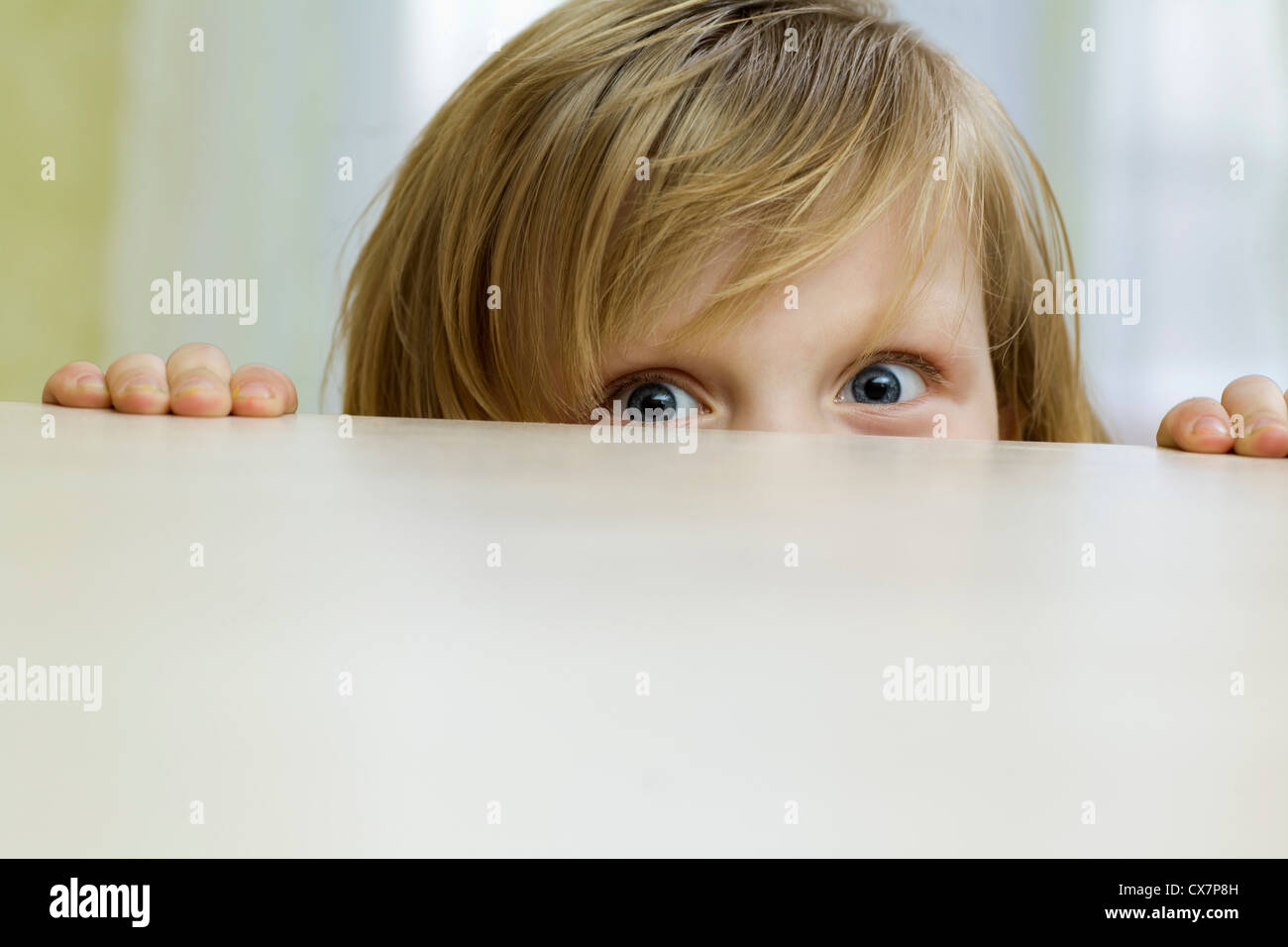 A mischievous girl peeking over the top of a table Stock Photo - Alamy