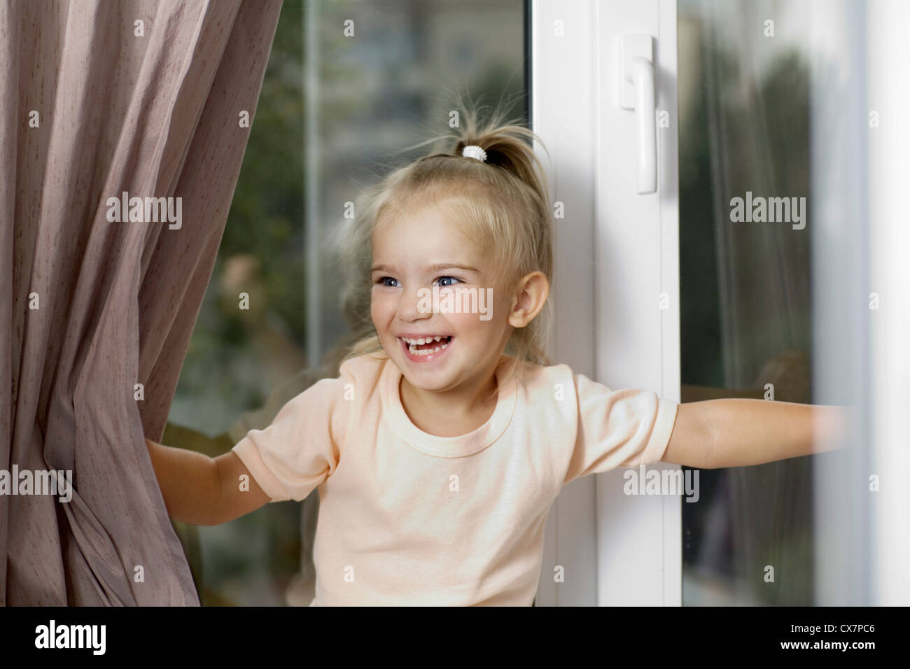A young laughing girl pushing window curtains apart Stock Photo - Alamy