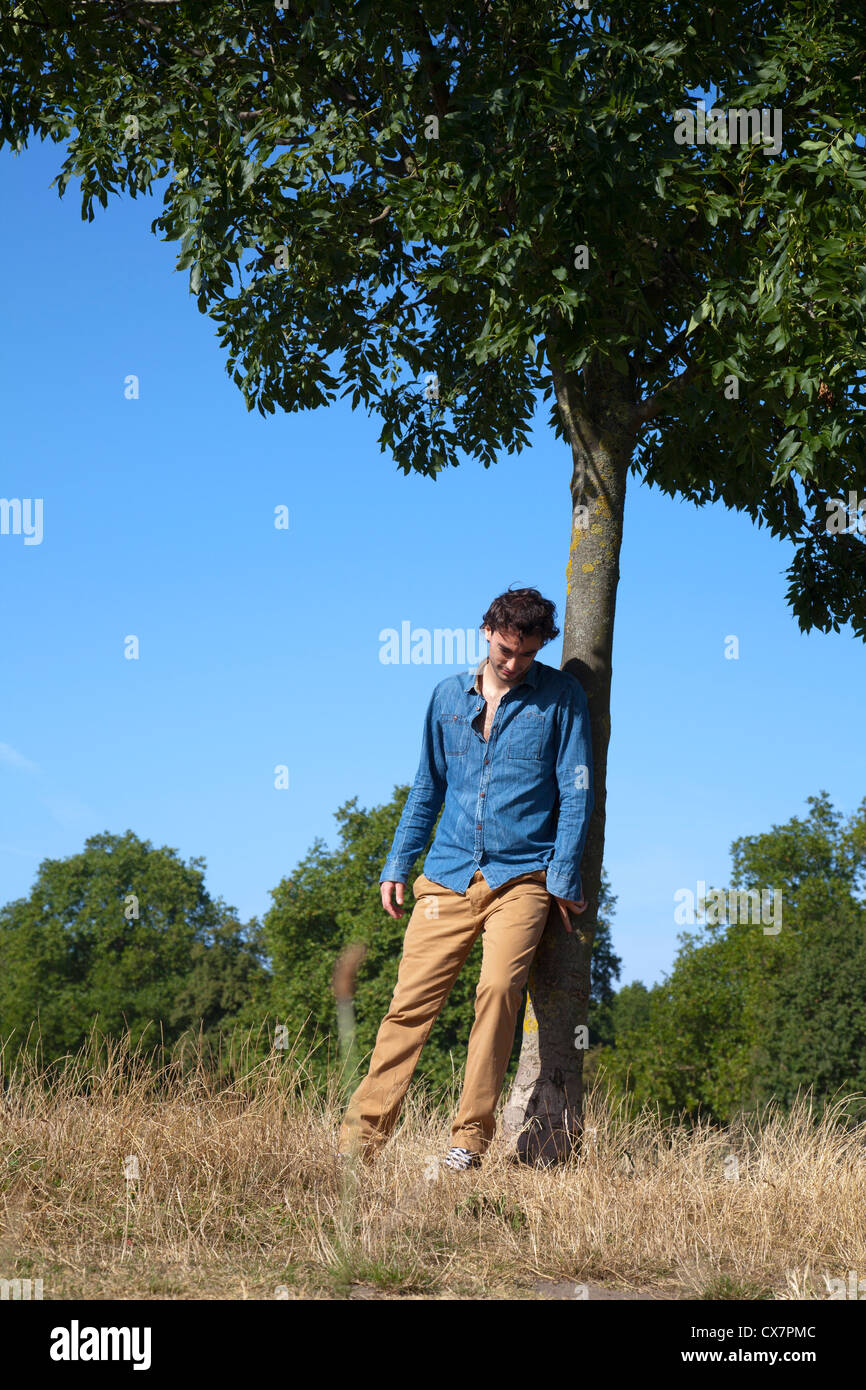 Man leaning against tree in park Stock Photo - Alamy