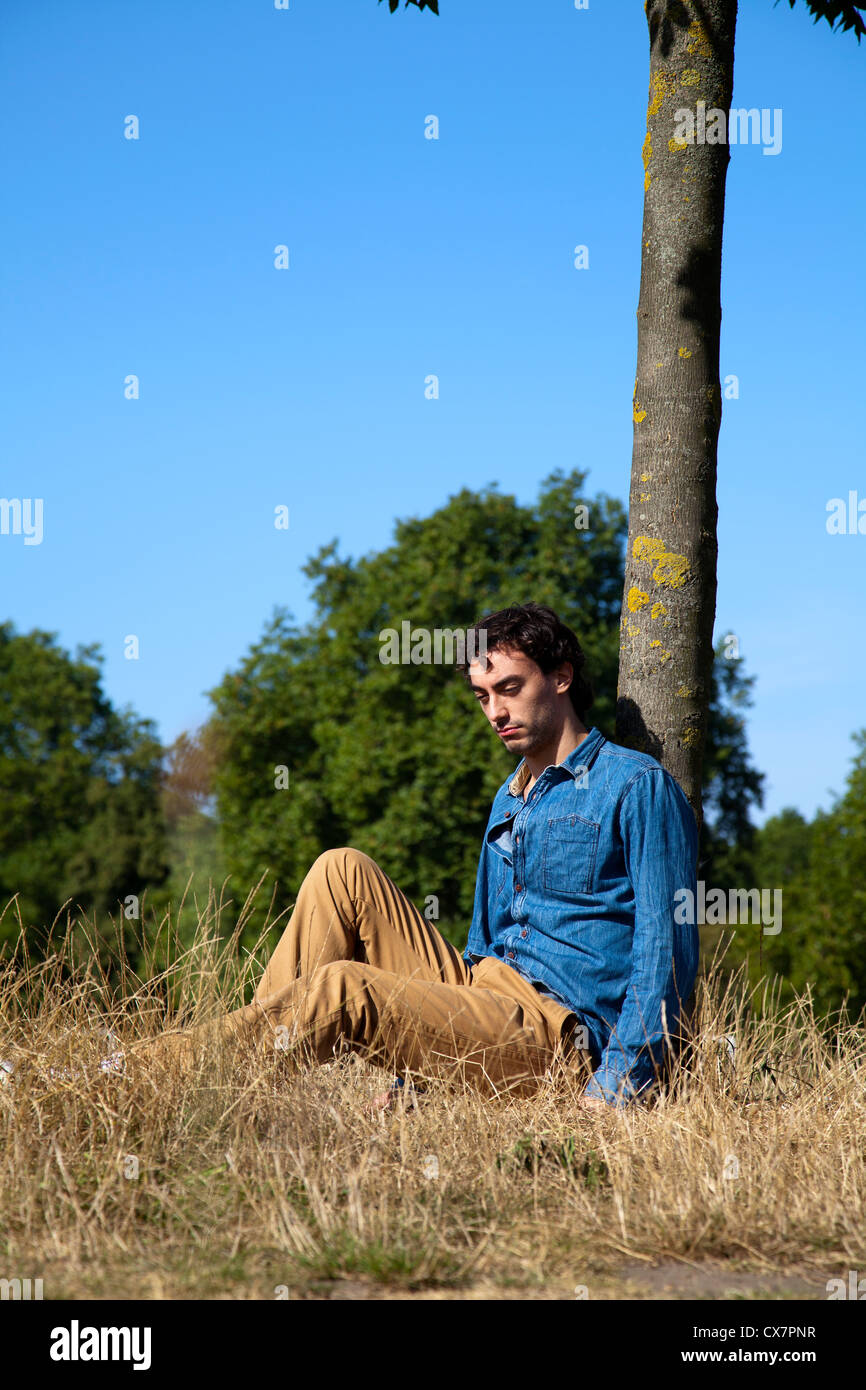 Man sitting against tree trunk in park Stock Photo - Alamy
