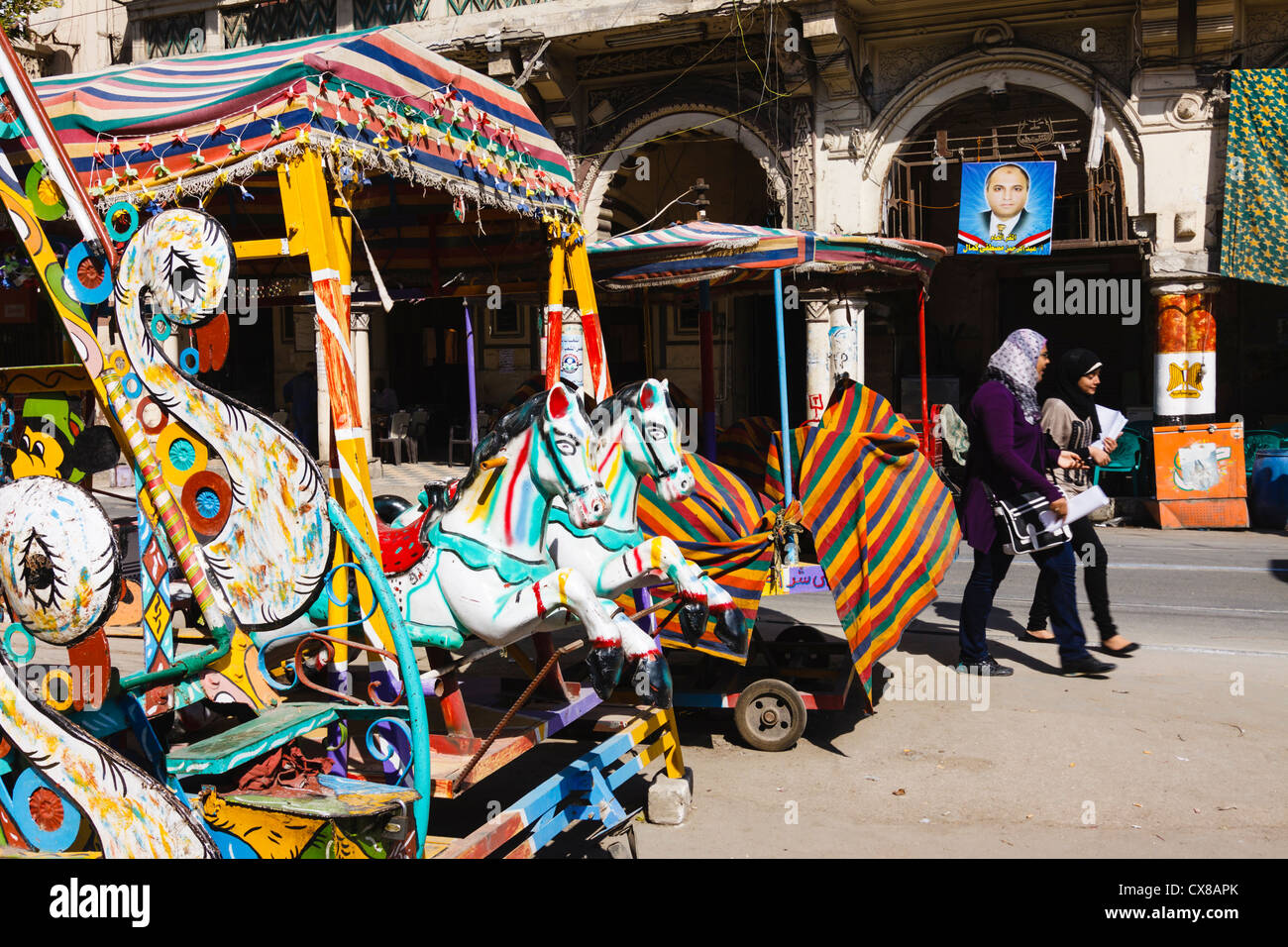 Veiled student girls walking by carousel horses in Anfushi old quarter ...