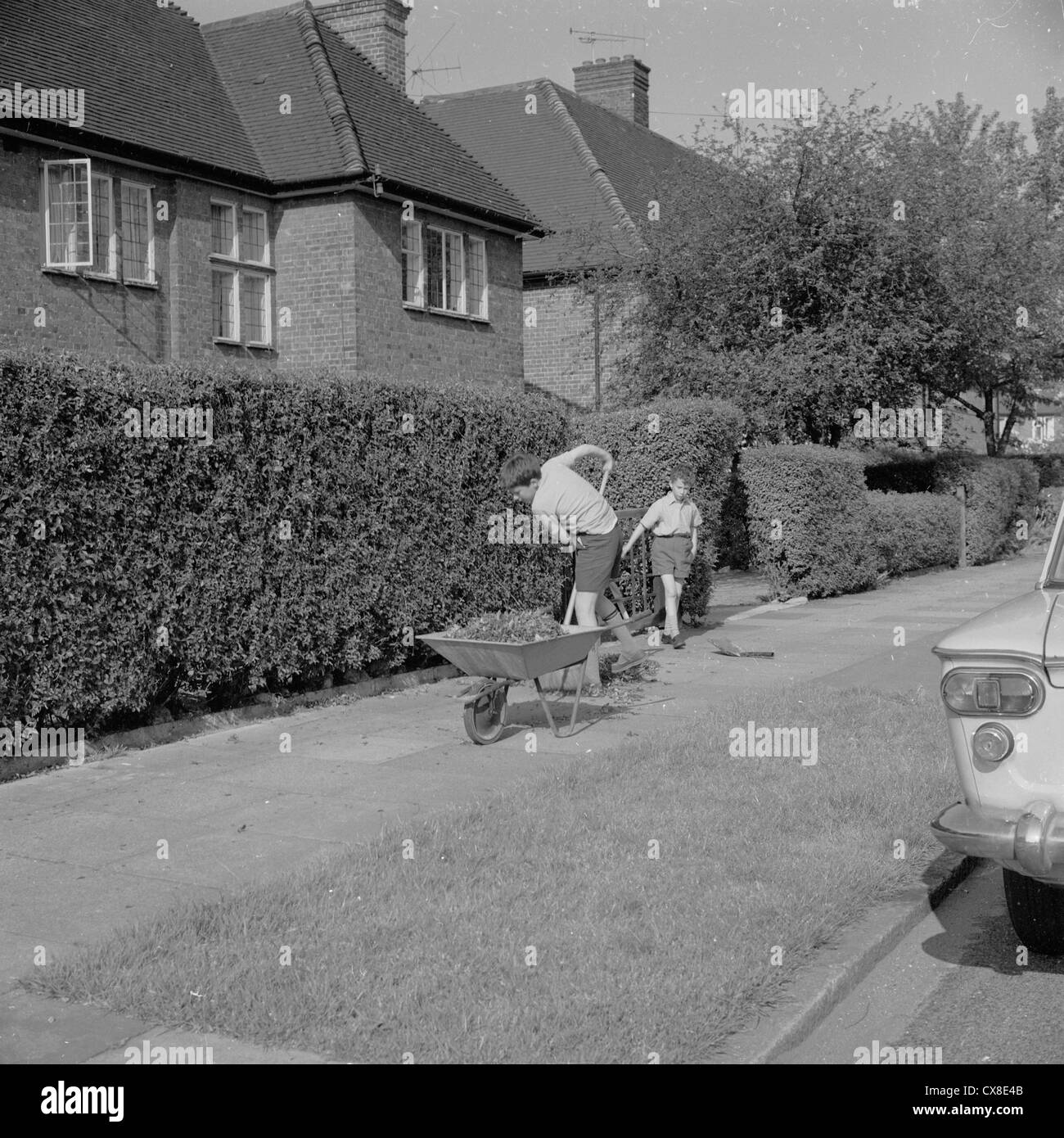 London,1950s. Children sweep up leaves on a pavement outside a smart ...