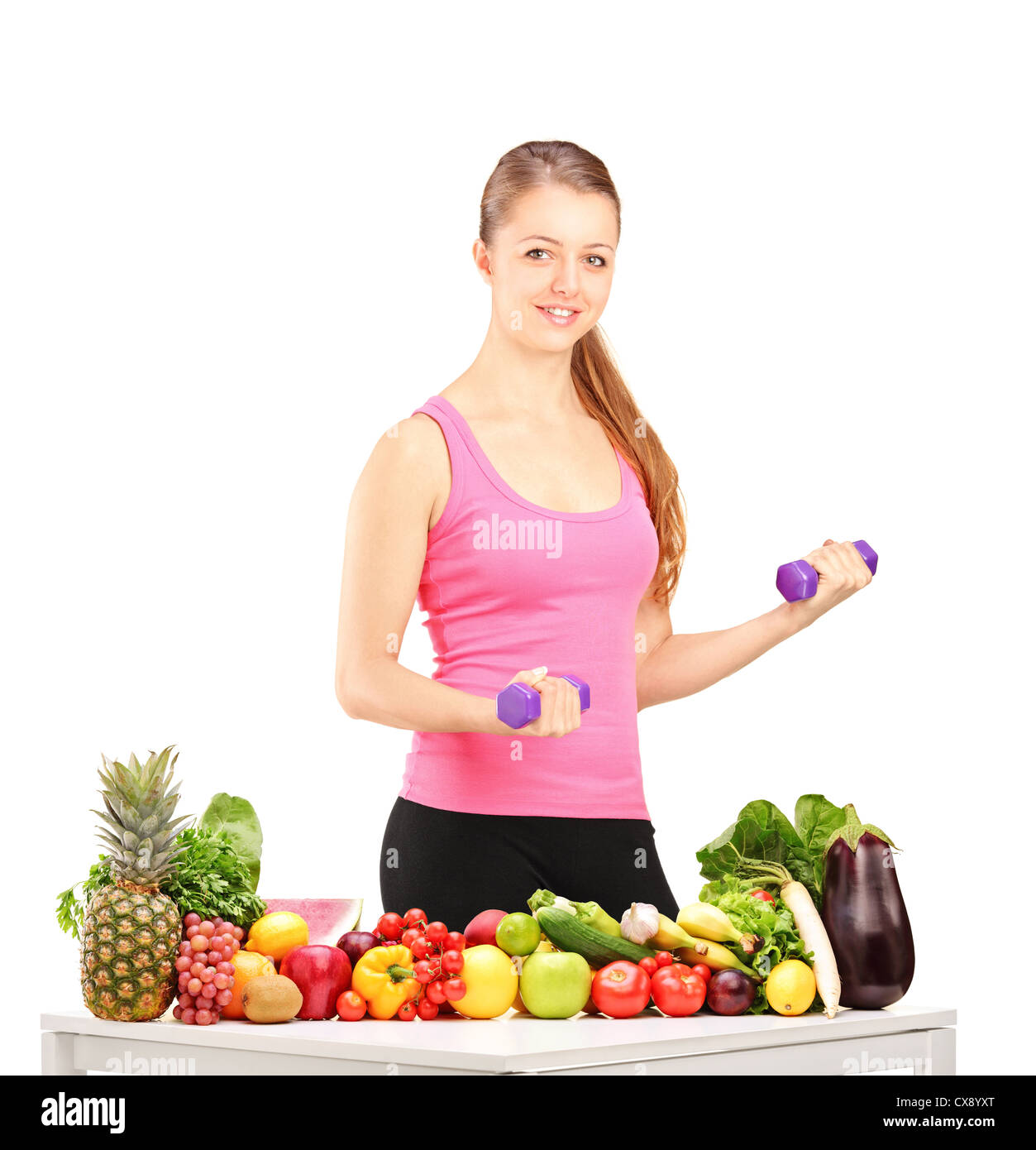 Smiling woman holding weights and table full of fruits and vegetables ...